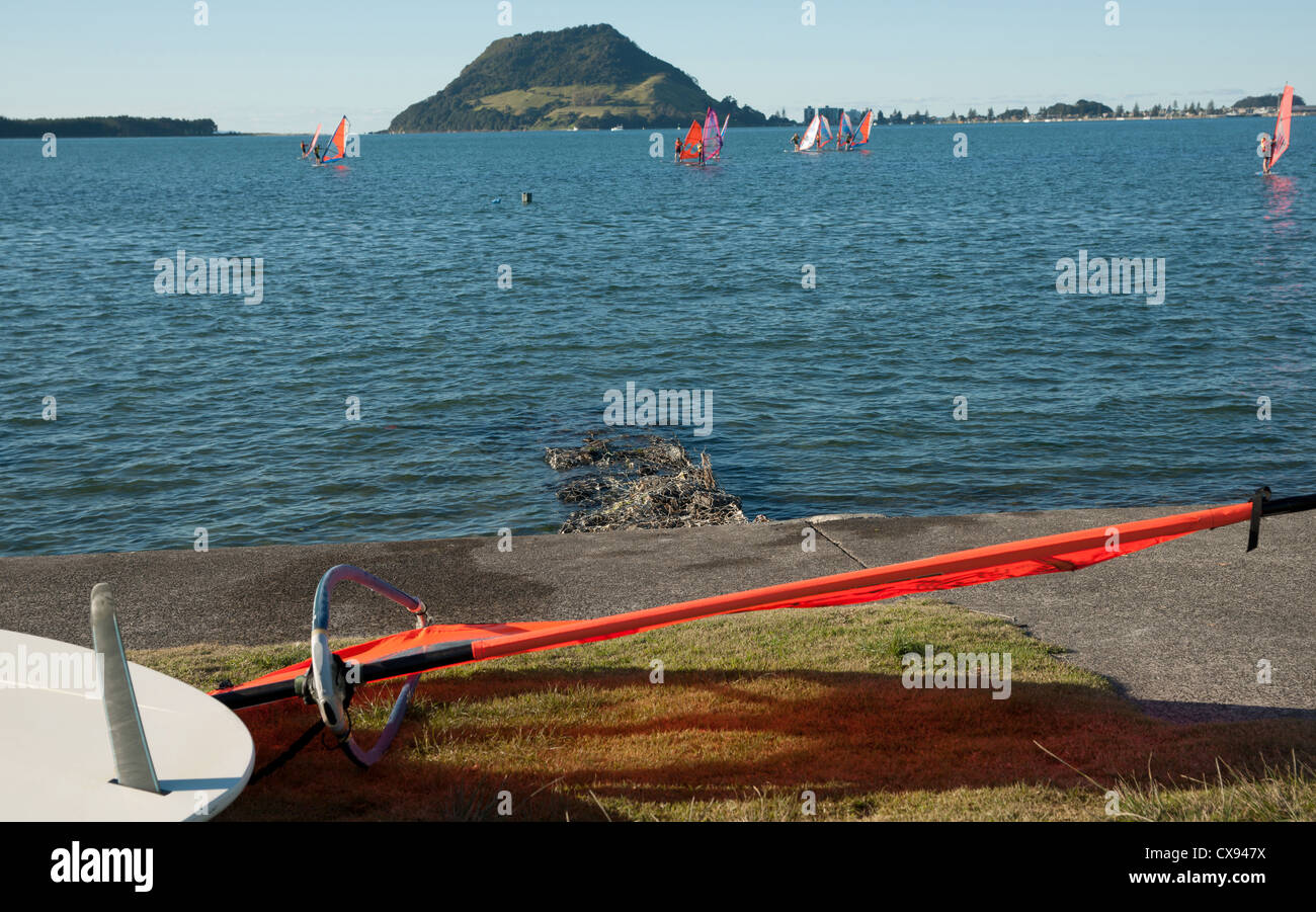 Windsurfers sailing on harbor, with board and sail on foreground beach ...