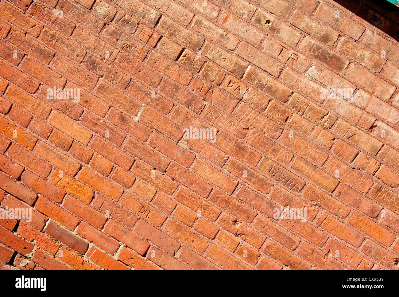 An old, red brick wall that has had many names carved into it Stock ...