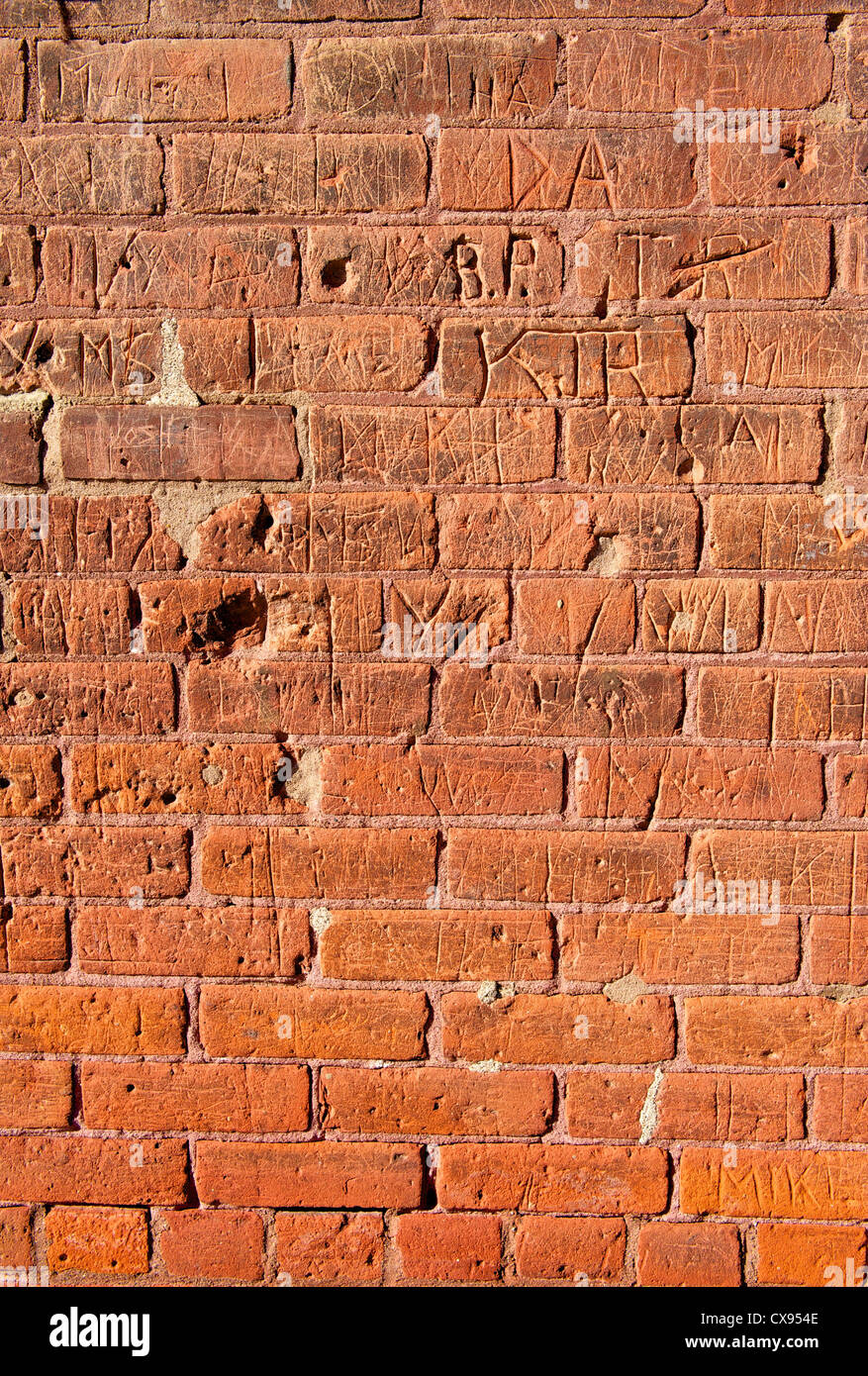 An old, red brick wall that has had many names carved into it Stock ...