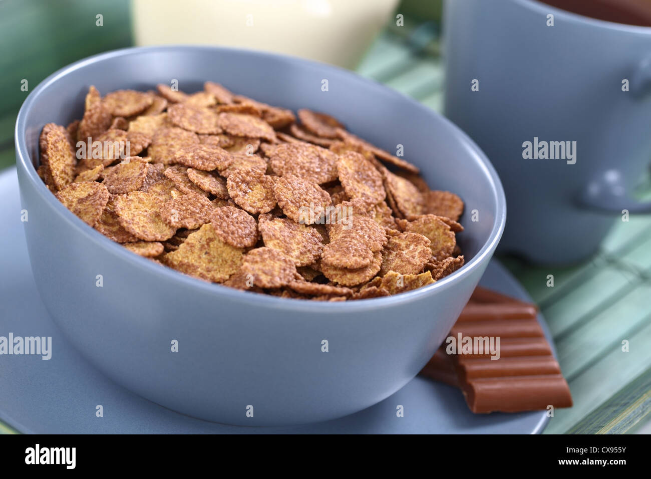 Bowl of chocolate corn flakes cereal with cup of coffee/tea and a jug ...