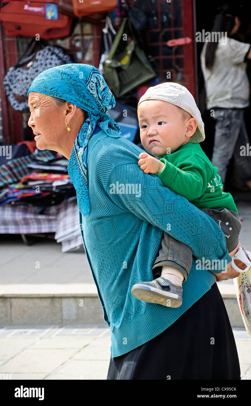 Grandmother carring her grandson on her back. Jeminay city Xinjiang ...
