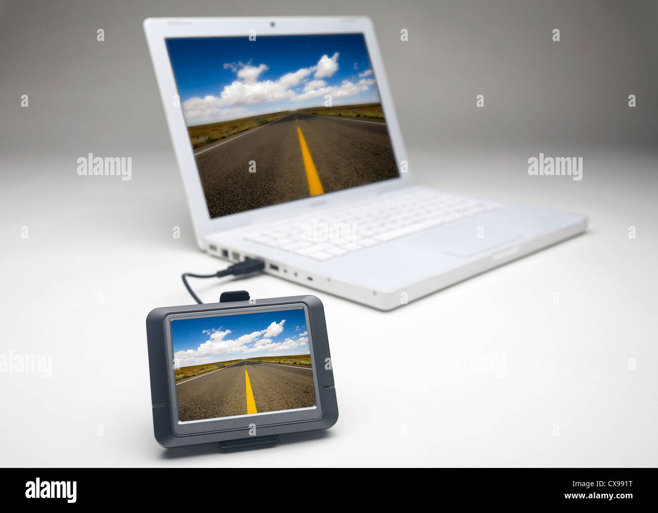 A GPS unit with a highway road picture is connected to a laptop ...