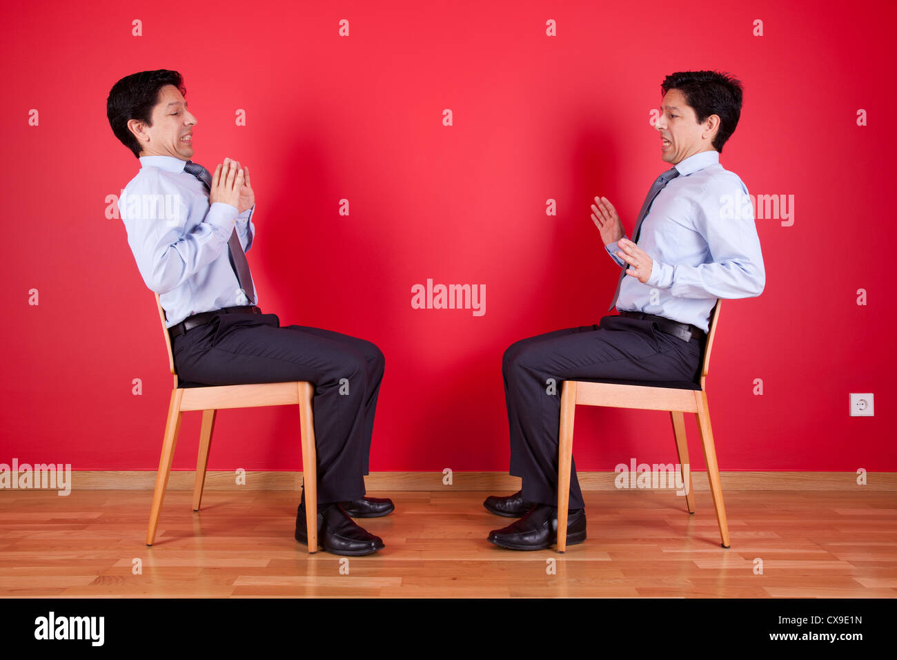 Confrontation between two twin businessman sited next to a red wall ...