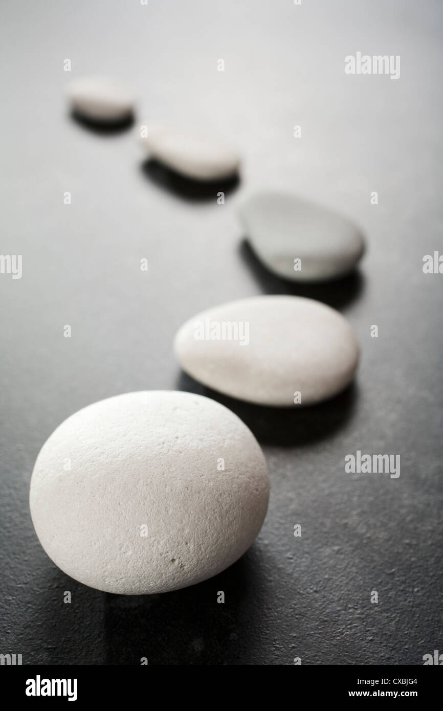 Curving line of light grey pebbles arranged on dark textured background ...