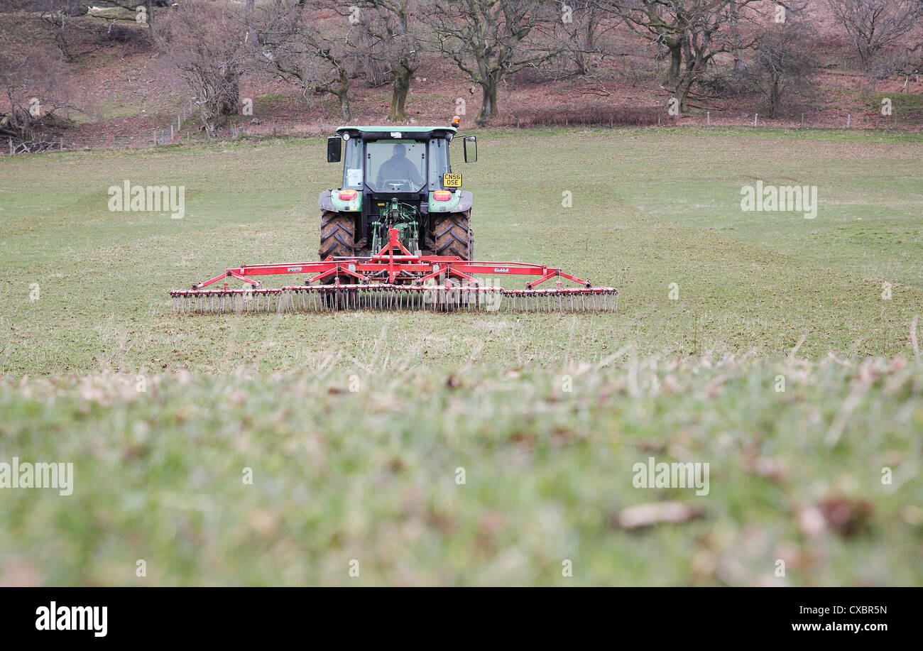 Farmer in tractor, aerating a field with grass harrows attachment on a ...