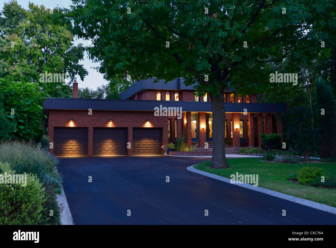 Red brick house with lights on and circular paved driveway and triple ...