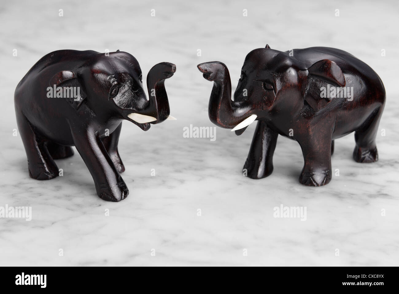 Two wood carved elephants with trunks raised on marble table signifying ...