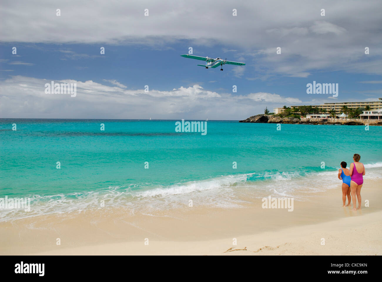 Two female beachgoers watch a plane land in St Maarten Maho Bay beach ...