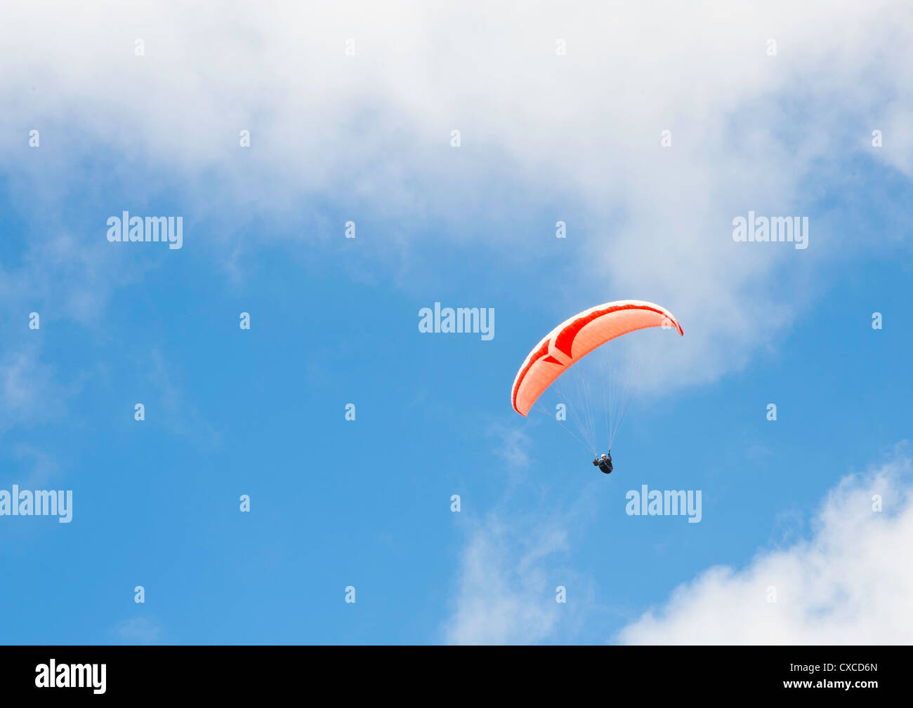 Single paraglider with a red and white parachute in flight beneath a ...