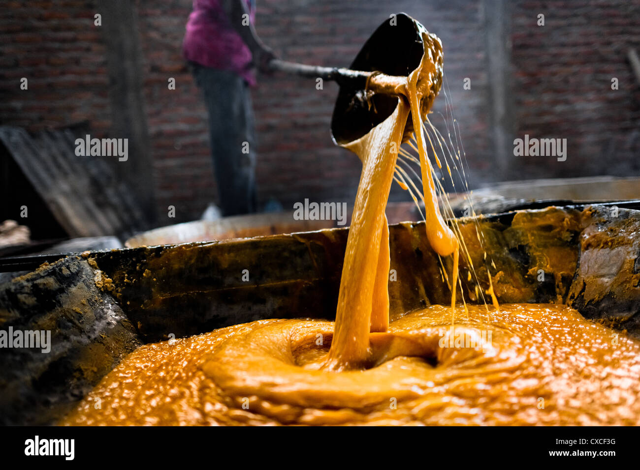 A Colombian peasant pours hot sugar cane juice into a cooking pot ...