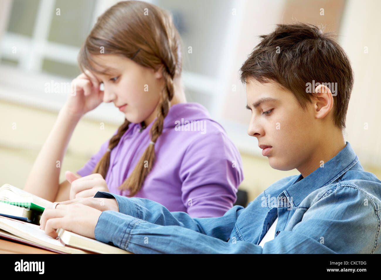 Portrait of teenage boy reading book with his classmate at background ...
