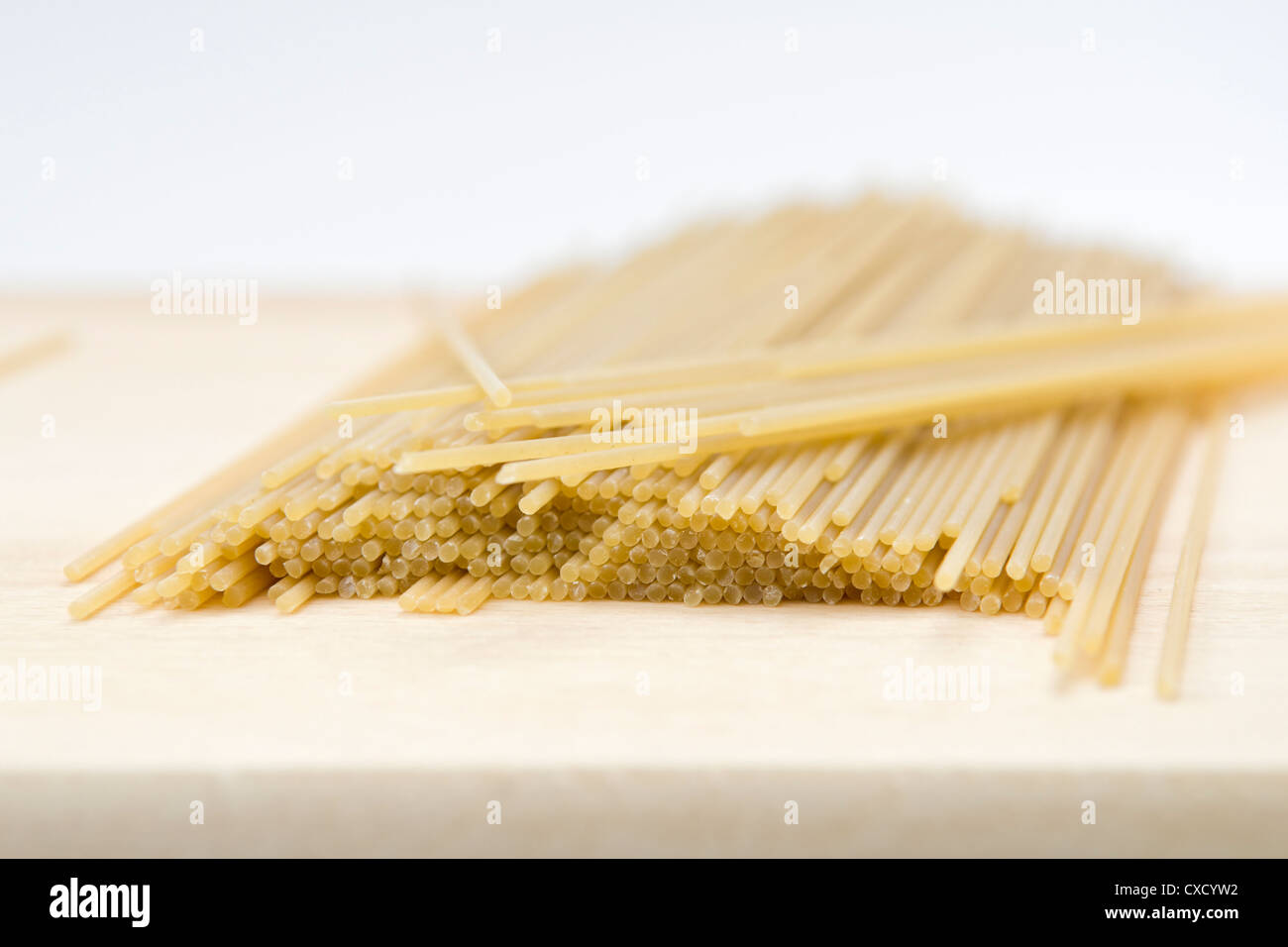 Spaghetti strands on wooden chopping board against a white background ...