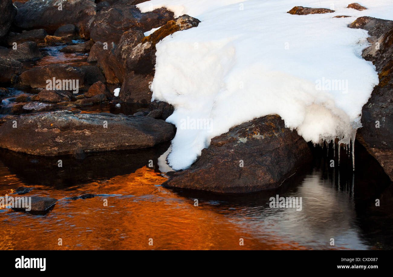 Warm light from the sun hitting rocks and snow around the edge of a ...