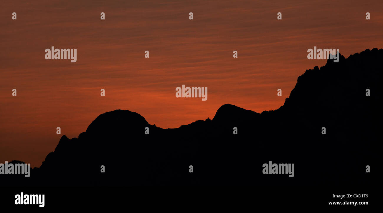 Silhouette of a mountainside at sunset against an orange sky, near ...