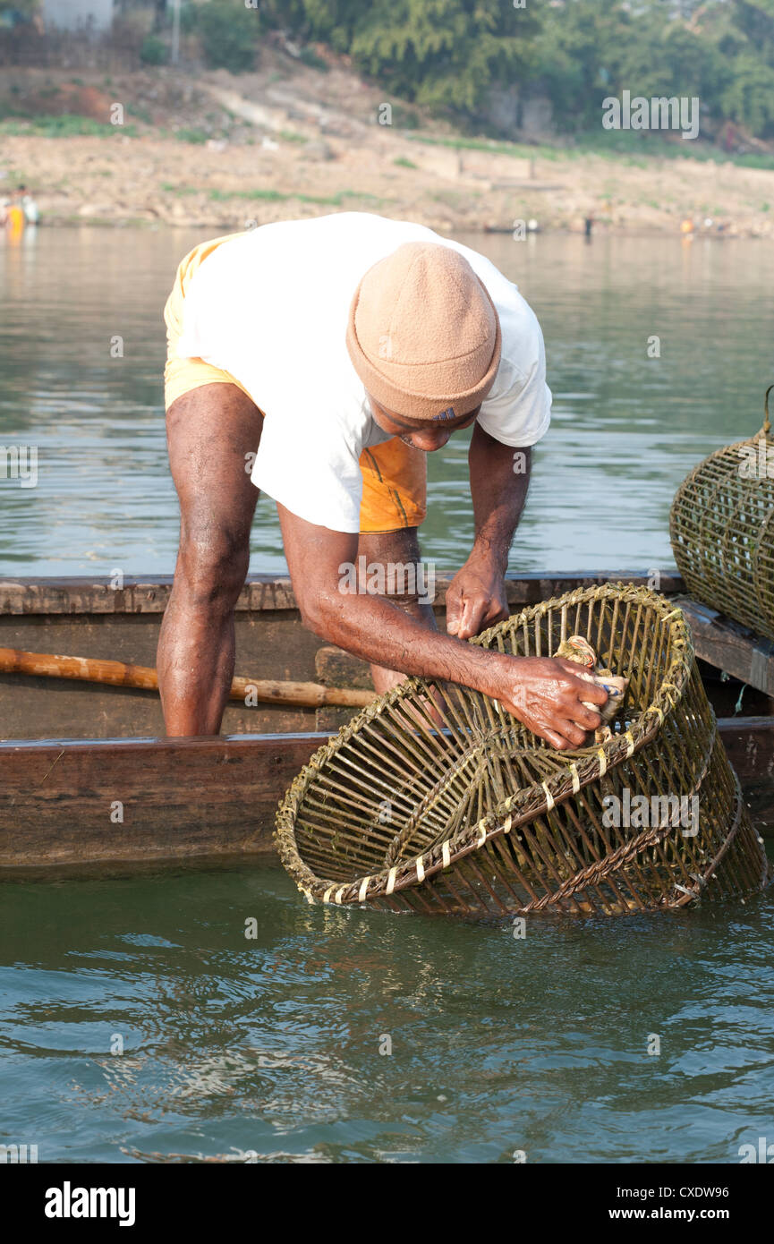 Fisherman in wooden boat, washing his coir and bamboo fishing pots ...