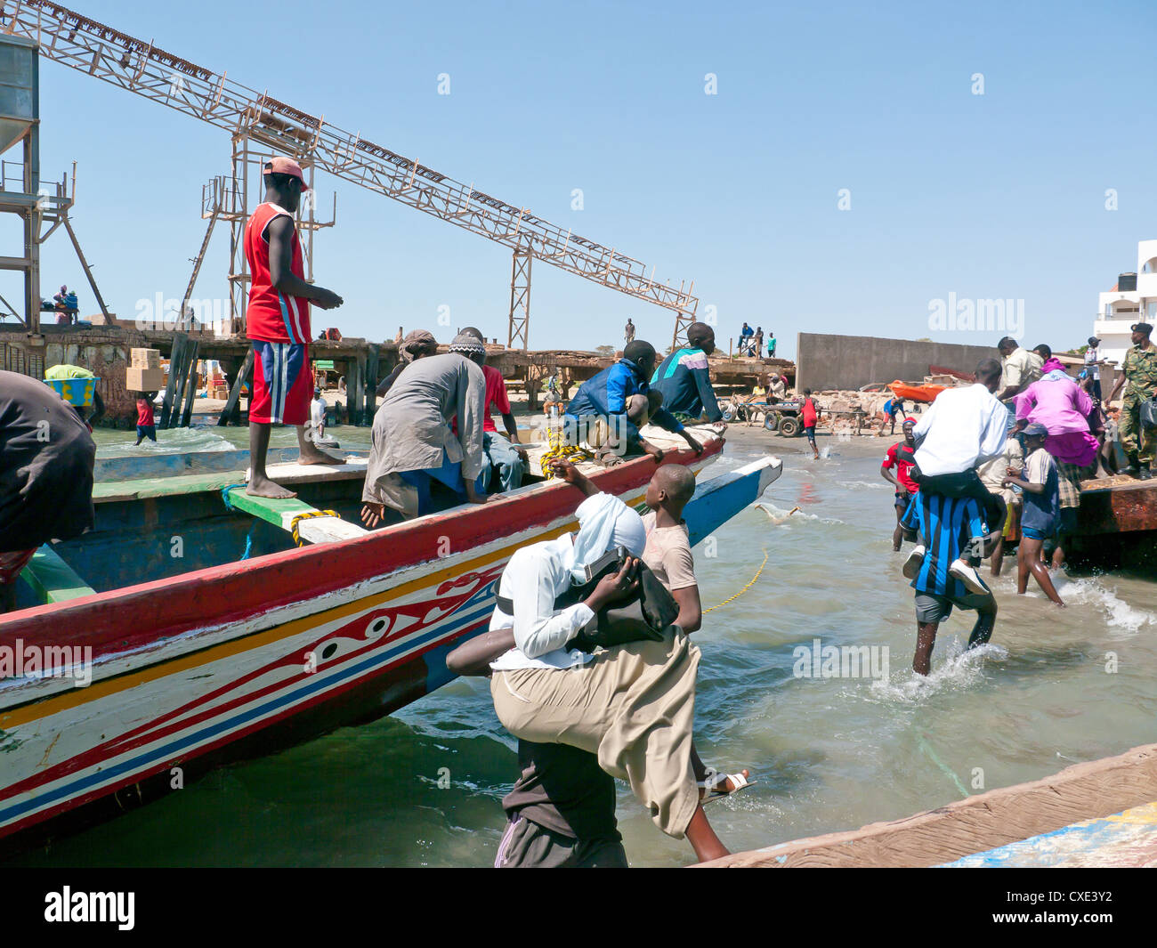 Men unloading passengers from a ferry on their shoulders on the beach ...