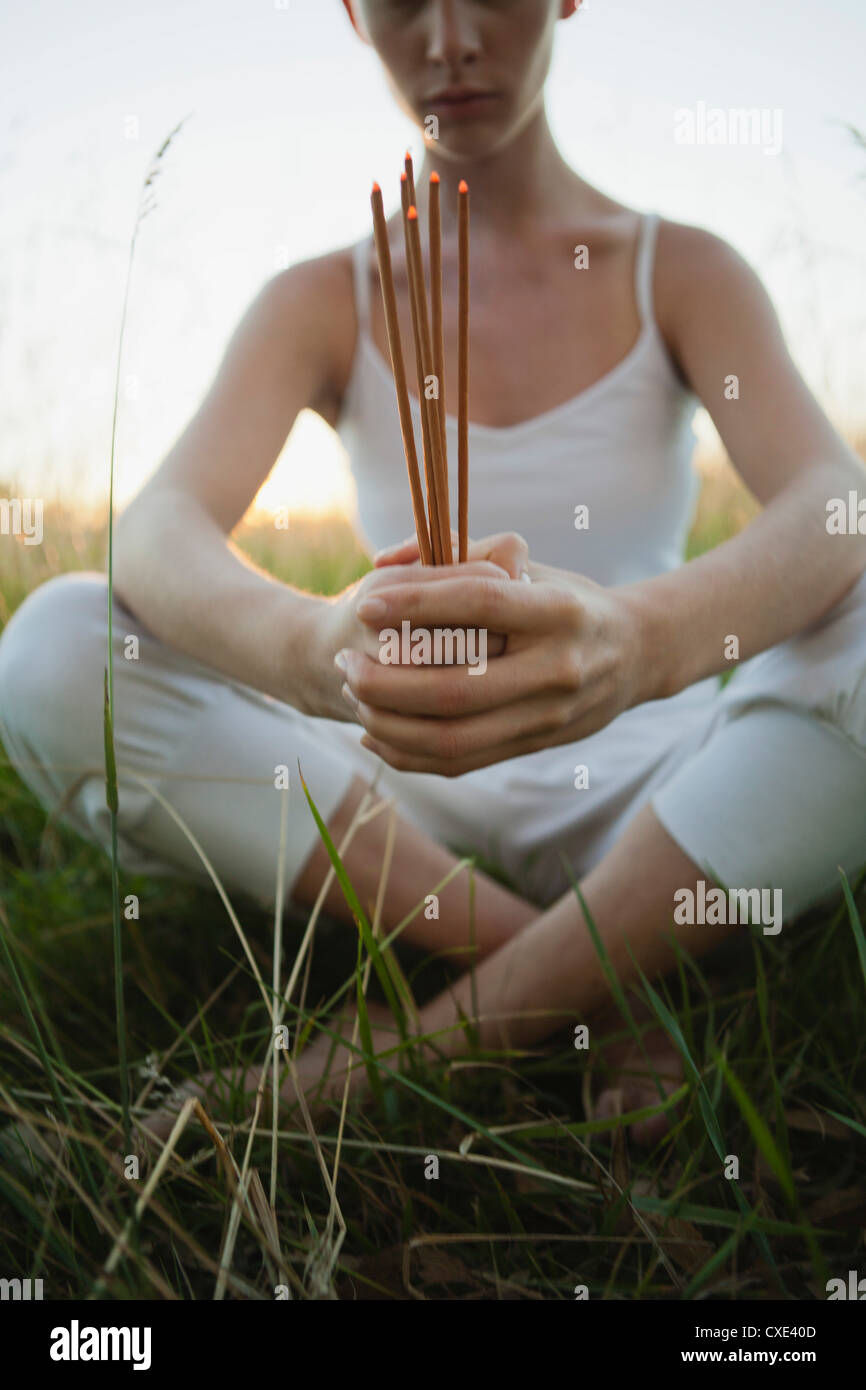 Young woman sitting in grass, holding incense sticks Stock Photo - Alamy
