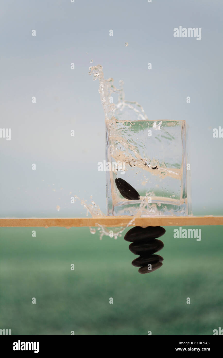 Stone falling in glass container, creating water splash, stack of ...