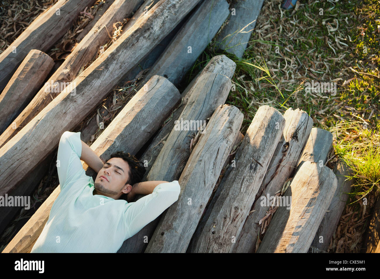 Young man lying on pile of logs, eyes closed Stock Photo - Alamy