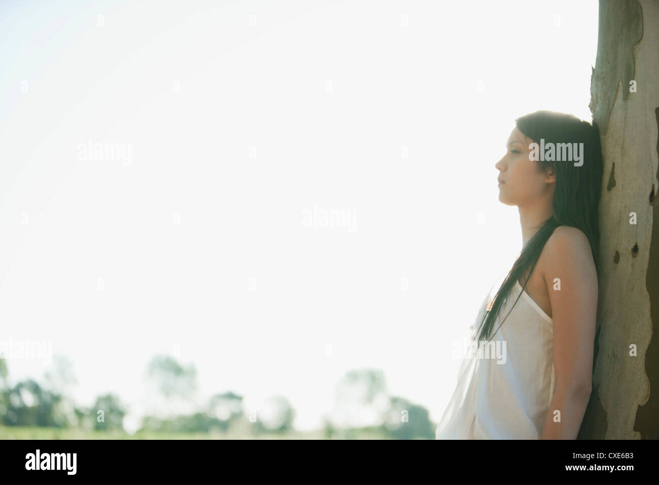 Young woman leaning aginst tree trunk, side view Stock Photo - Alamy