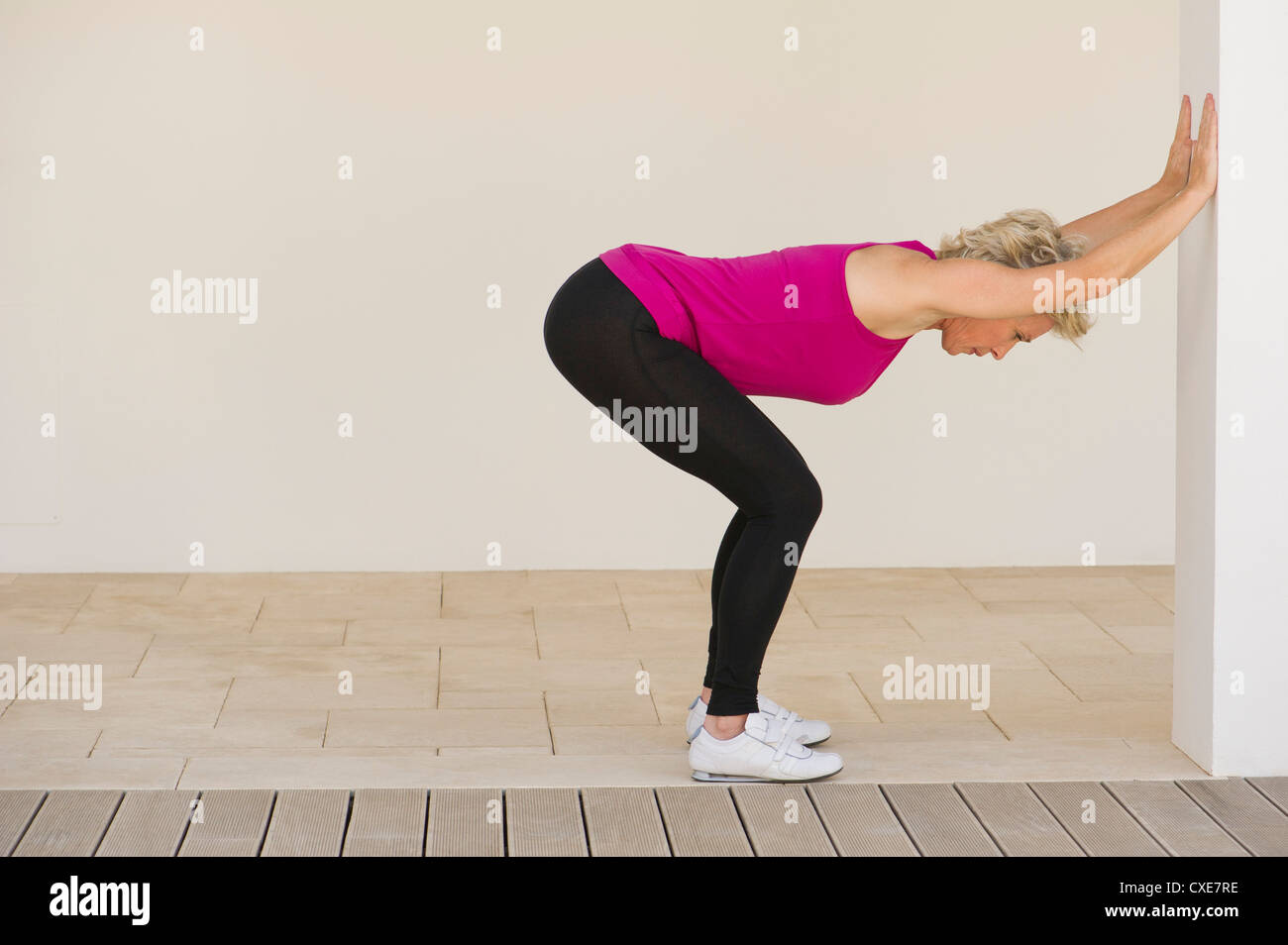 Mature woman stretching against wall, side view Stock Photo - Alamy