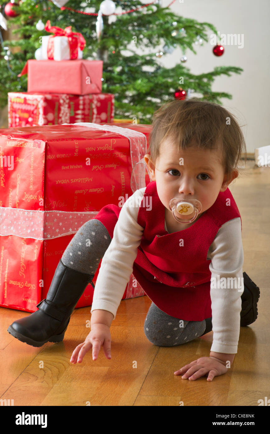 Baby girl crouching in front of Christmas presents Stock Photo - Alamy