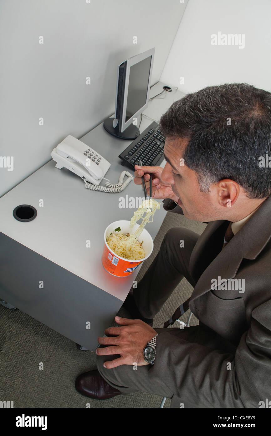 Businessman eating ramen noodles at desk in office Stock Photo - Alamy