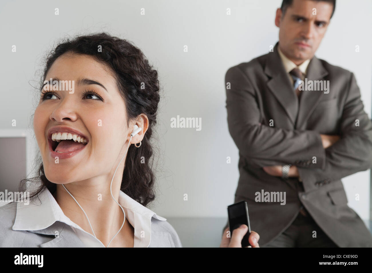 Woman distractedly listening to MP3 player at work, boss glaring in ...