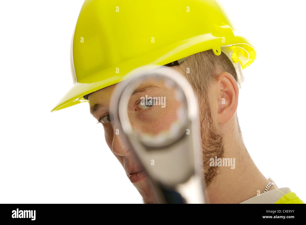 Young apprentice workman looking through ring spanner with hard hat on ...