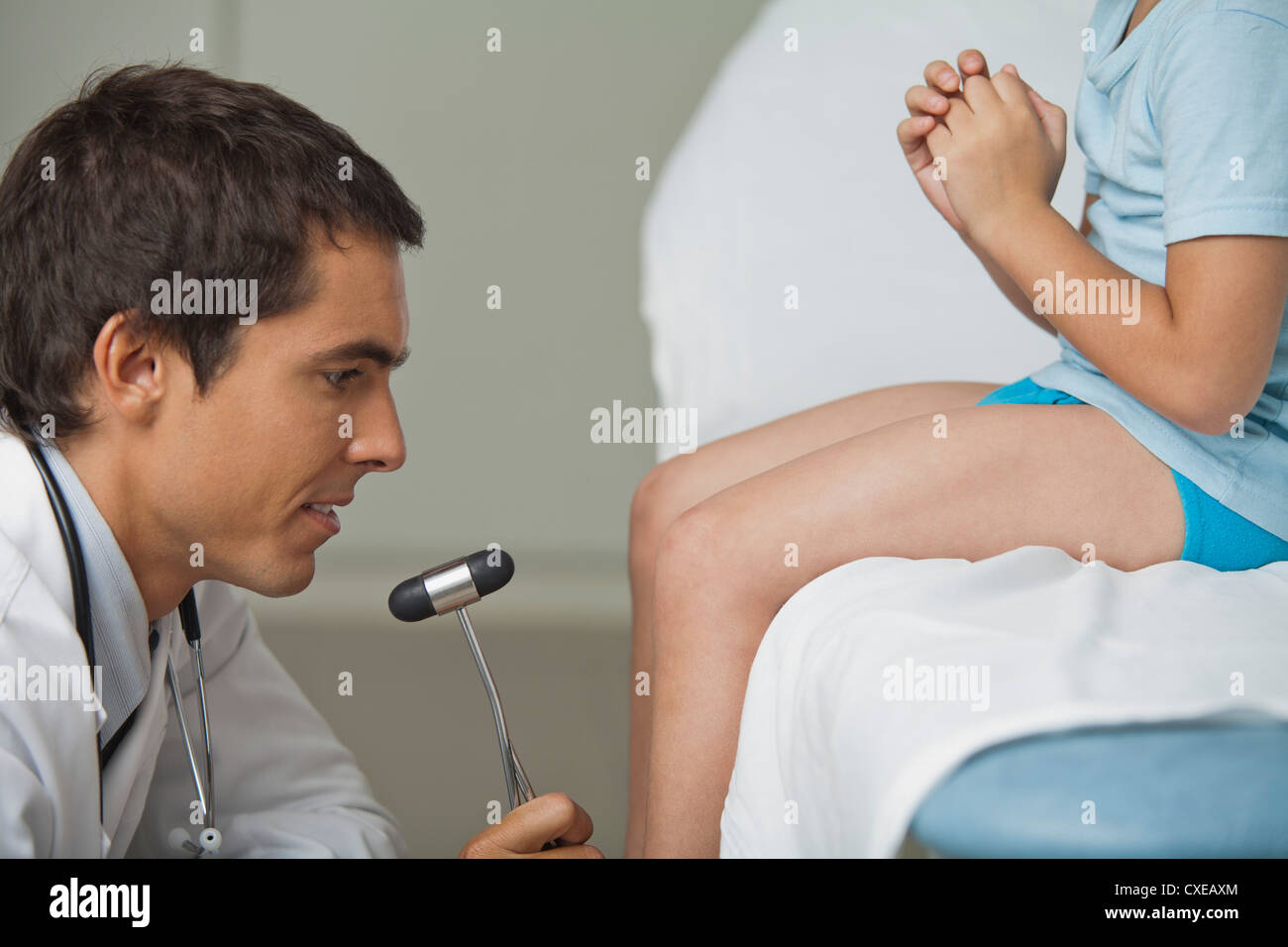 Doctor checking boy's reflexes with reflex hammer, side view, cropped ...
