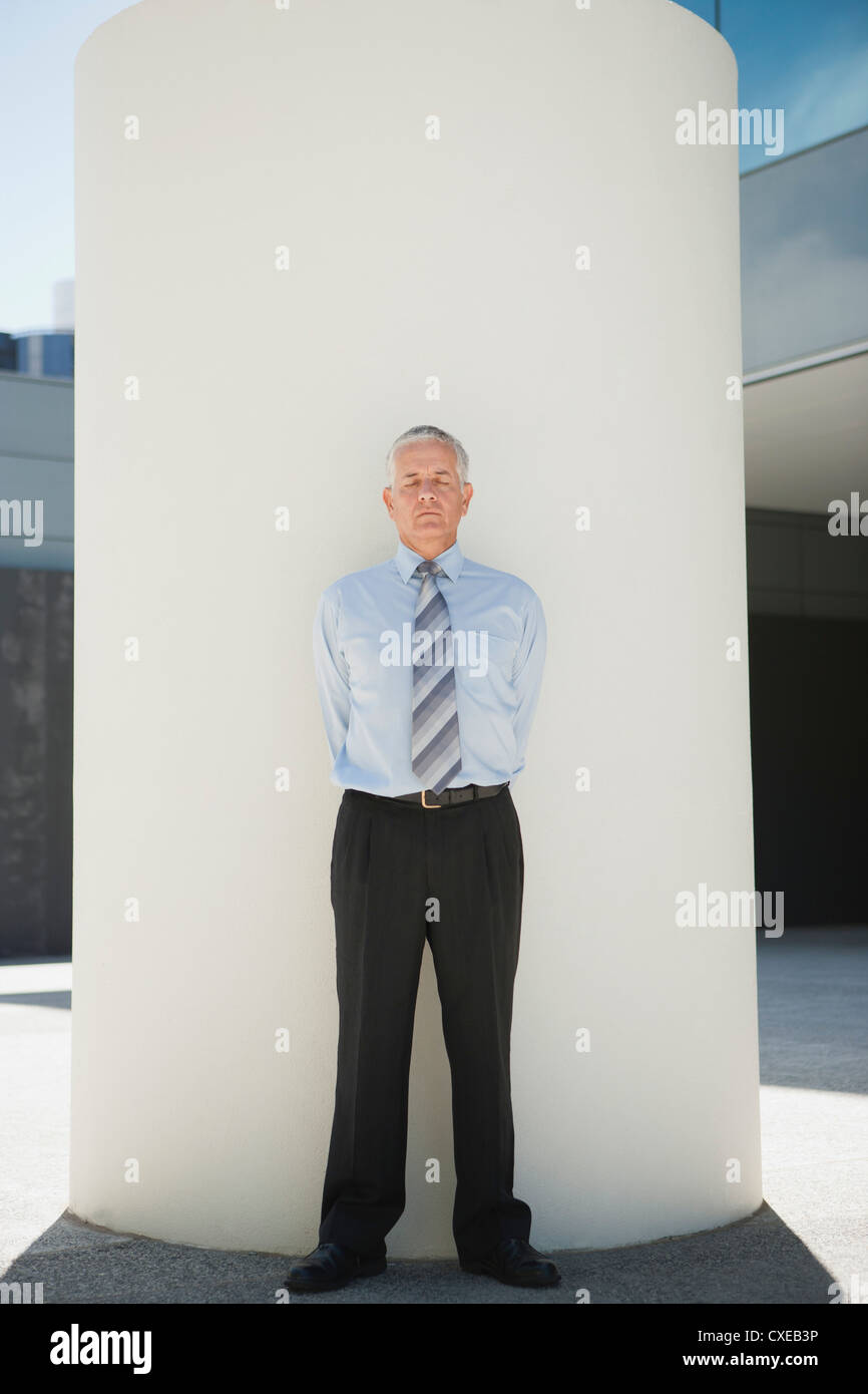 Mature businessman leaning against column with eyes closed Stock Photo ...