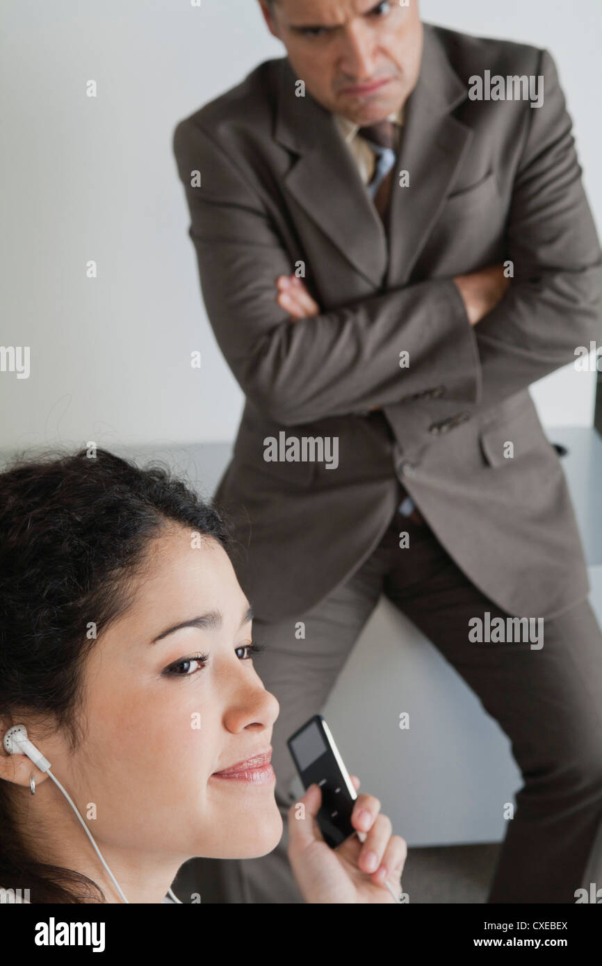 Woman distractedly listening to MP3 player at work, angry boss in ...