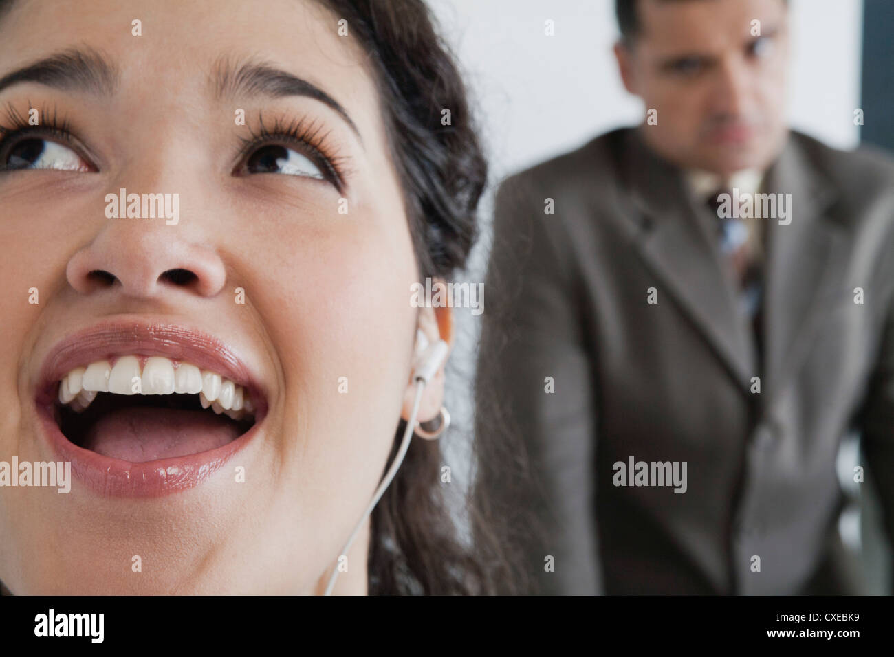Woman listening to earphones and singing in office, angry boss in ...