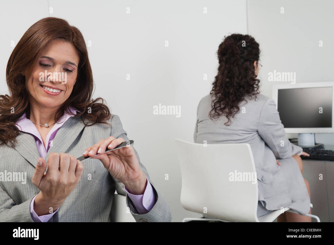Woman filing her nails in office, colleague working in background Stock ...