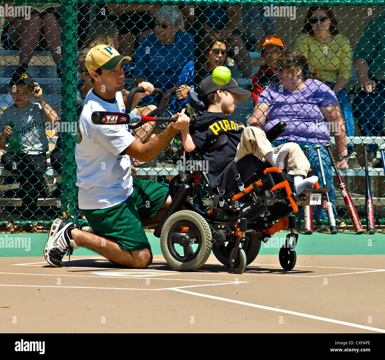 A young boy in wheel chair playing softball with the help of an adult ...