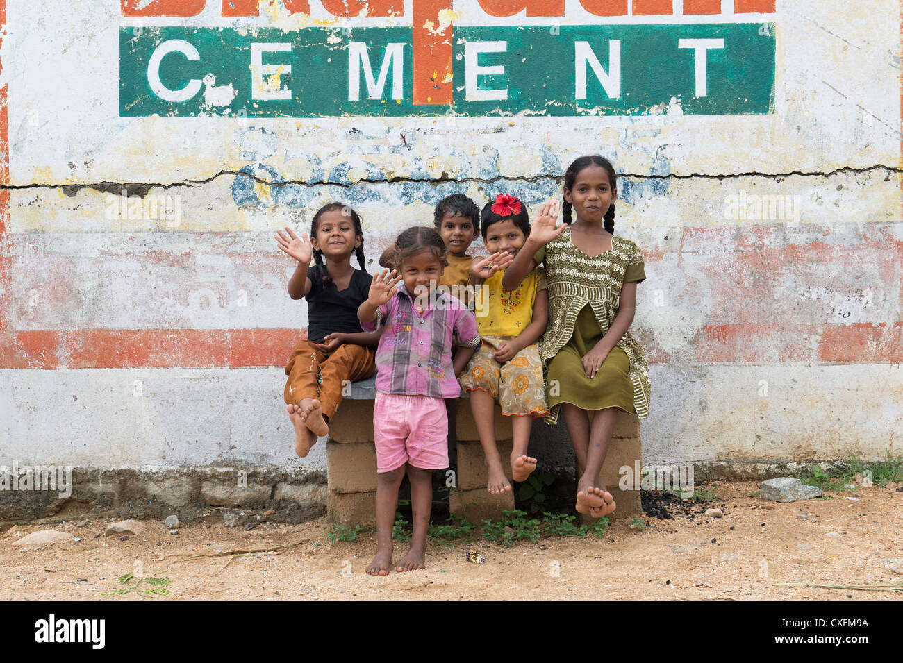 Happy young rural Indian village children sitting against a wall waving ...