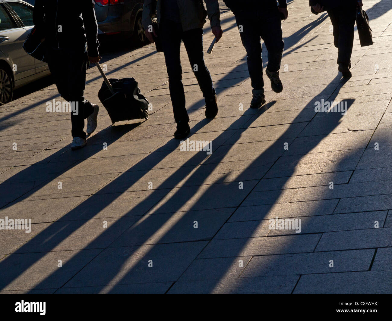 Commuters walking on city pavement with long shadows cast by late ...