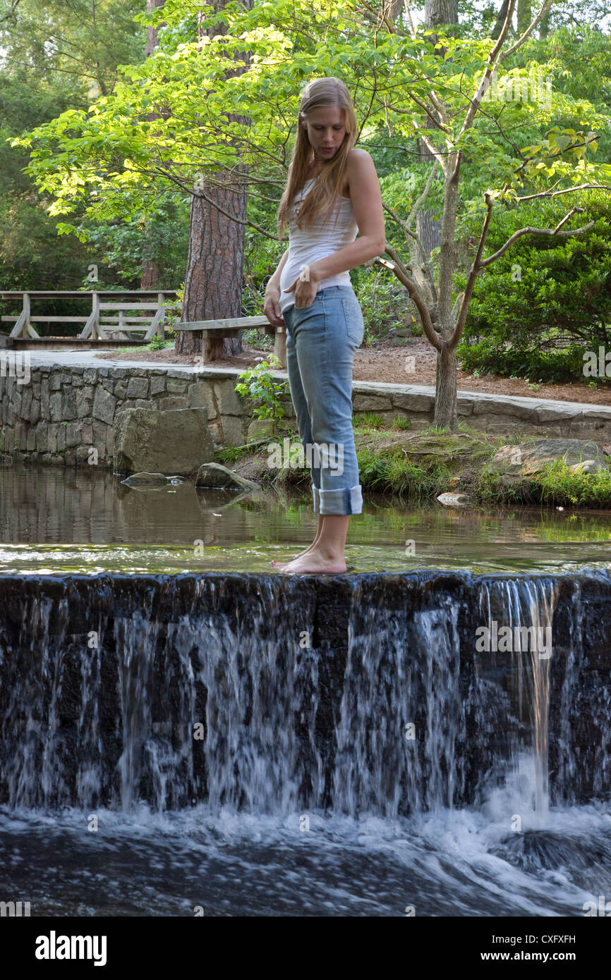 Pretty blond Caucasian woman outside, standing on top of a dam as water ...