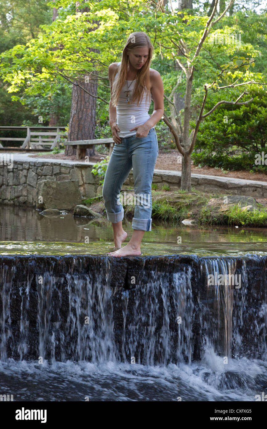 Pretty blond Caucasian woman outside, standing on top of a dam as water ...