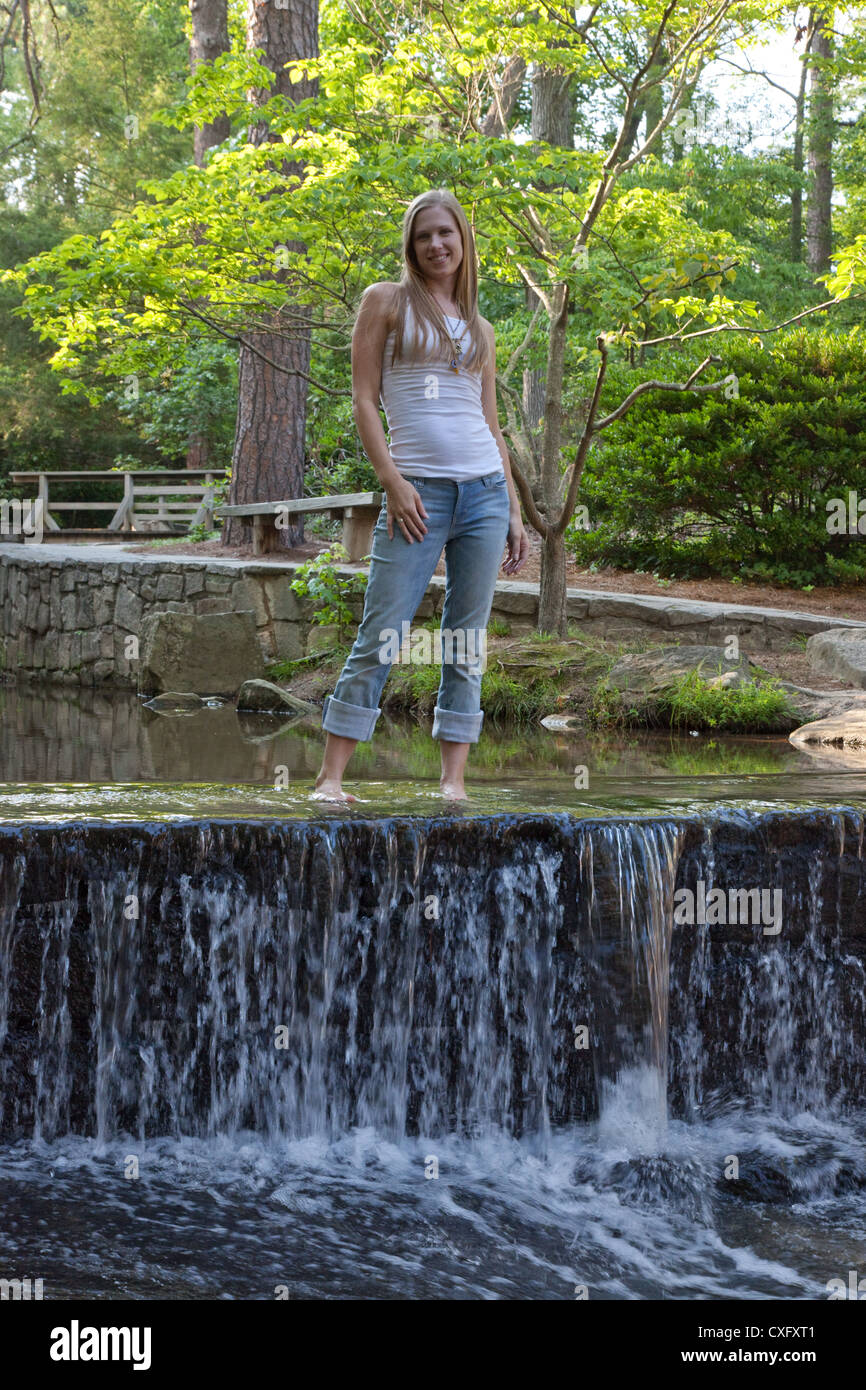 Pretty blond Caucasian woman outside, standing on top of a dam as water ...