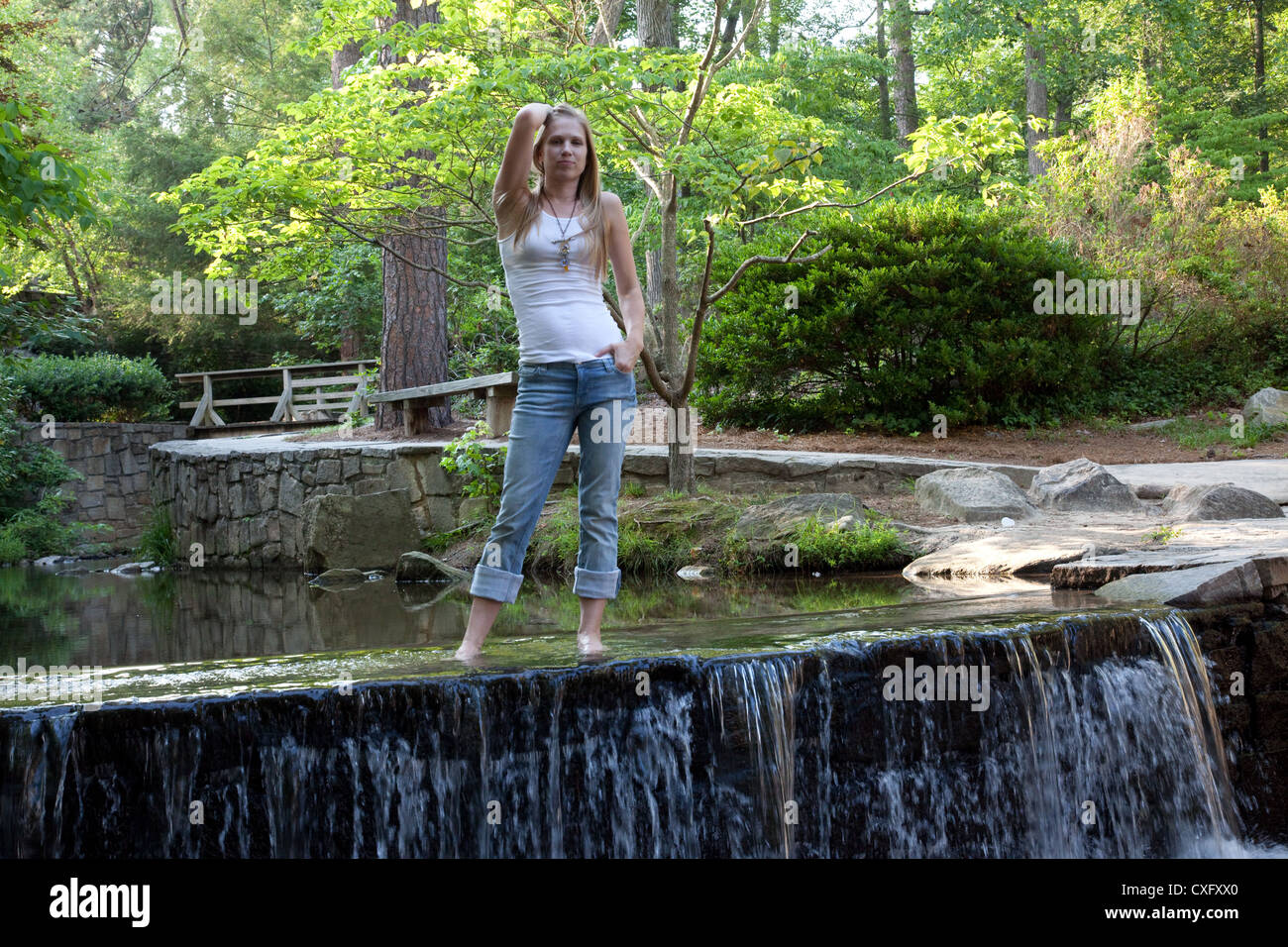 Pretty blond Caucasian woman outside, standing on top of a dam as water ...