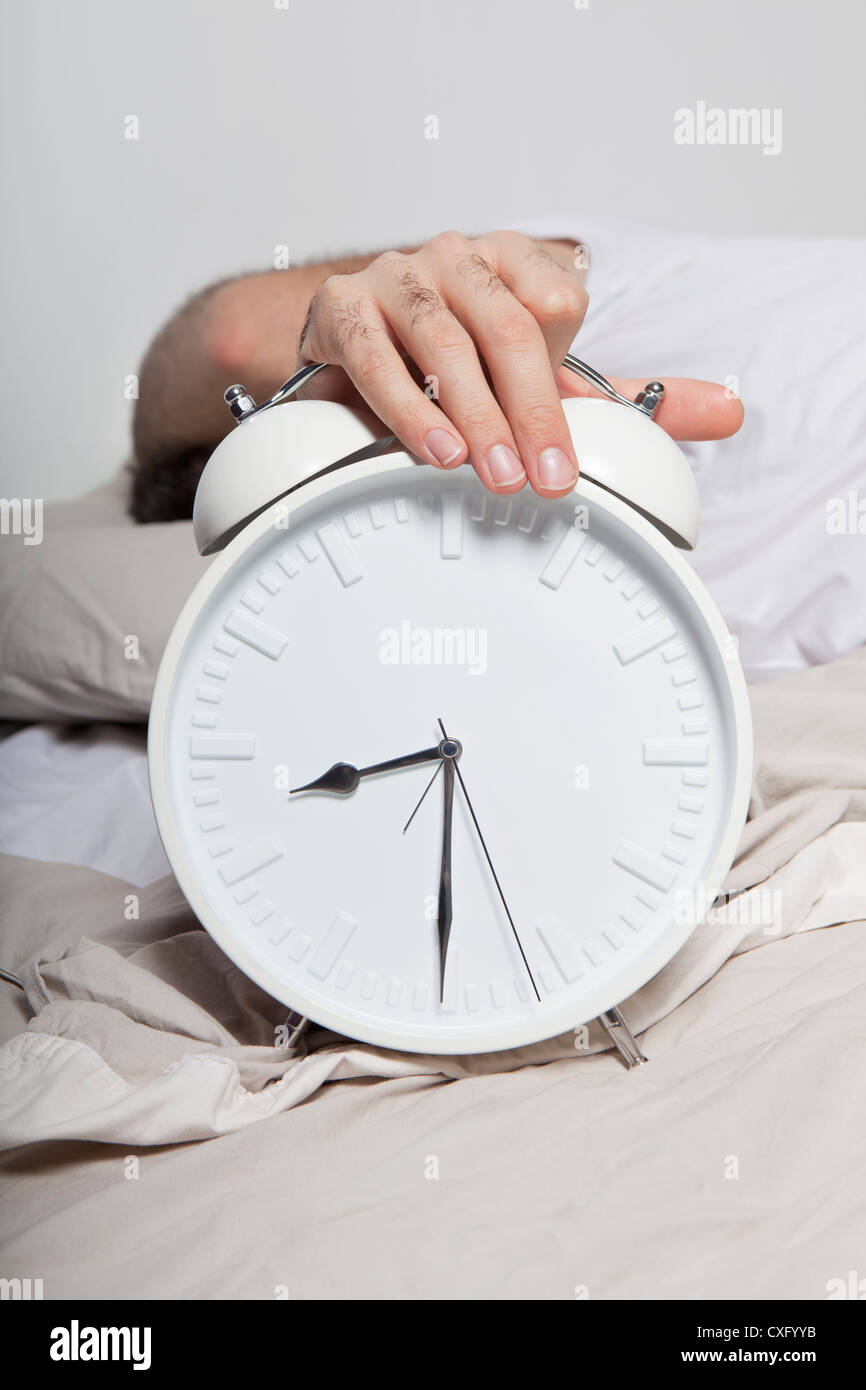 A man laying in a bed and holding a big white alarm clock Stock Photo ...