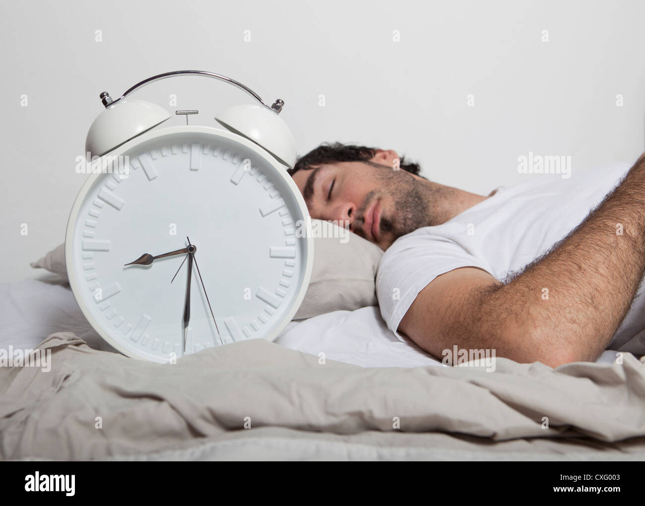 A man laying in a bed with a big white alarm clock Stock Photo - Alamy