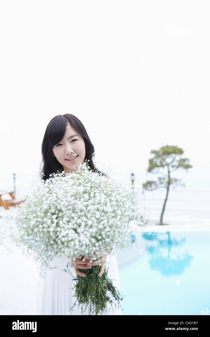A woman holding a bucay of with flowers with a tree in the backgound ...