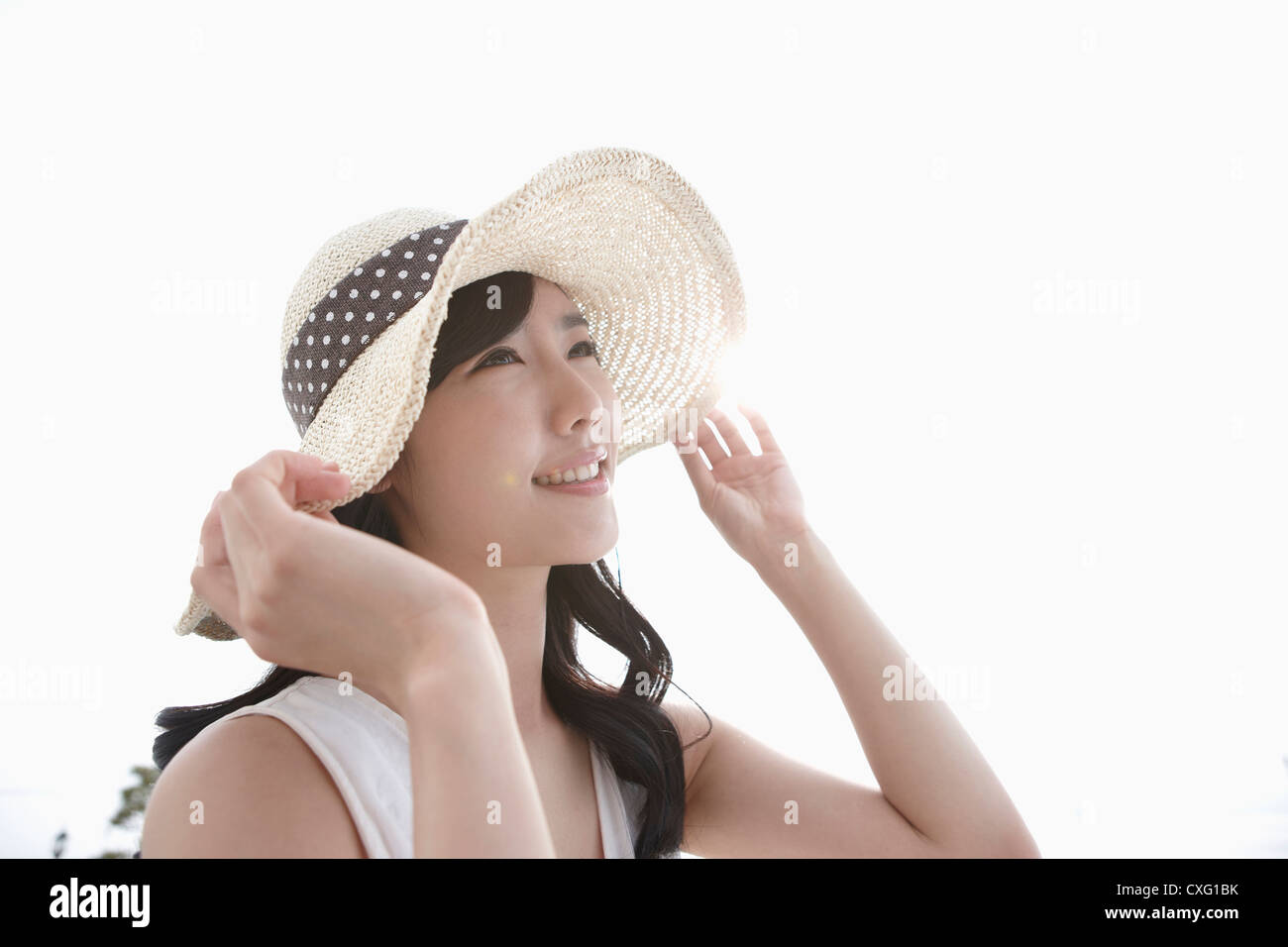 A woman wearing a white dress and straw hat grabbing her hat with both ...