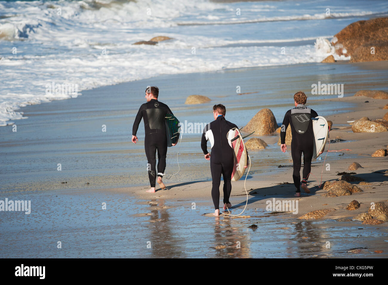 Three surfers walking along the beach at Sennen in Cornwall Stock Photo ...