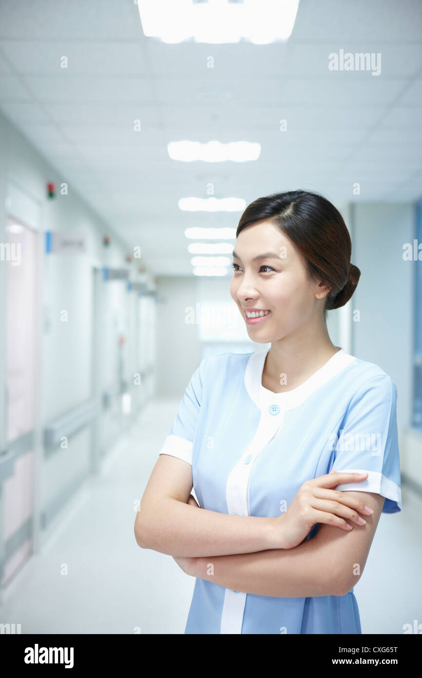 A nurse standing side ways in an empty hospital corridor with her arms ...