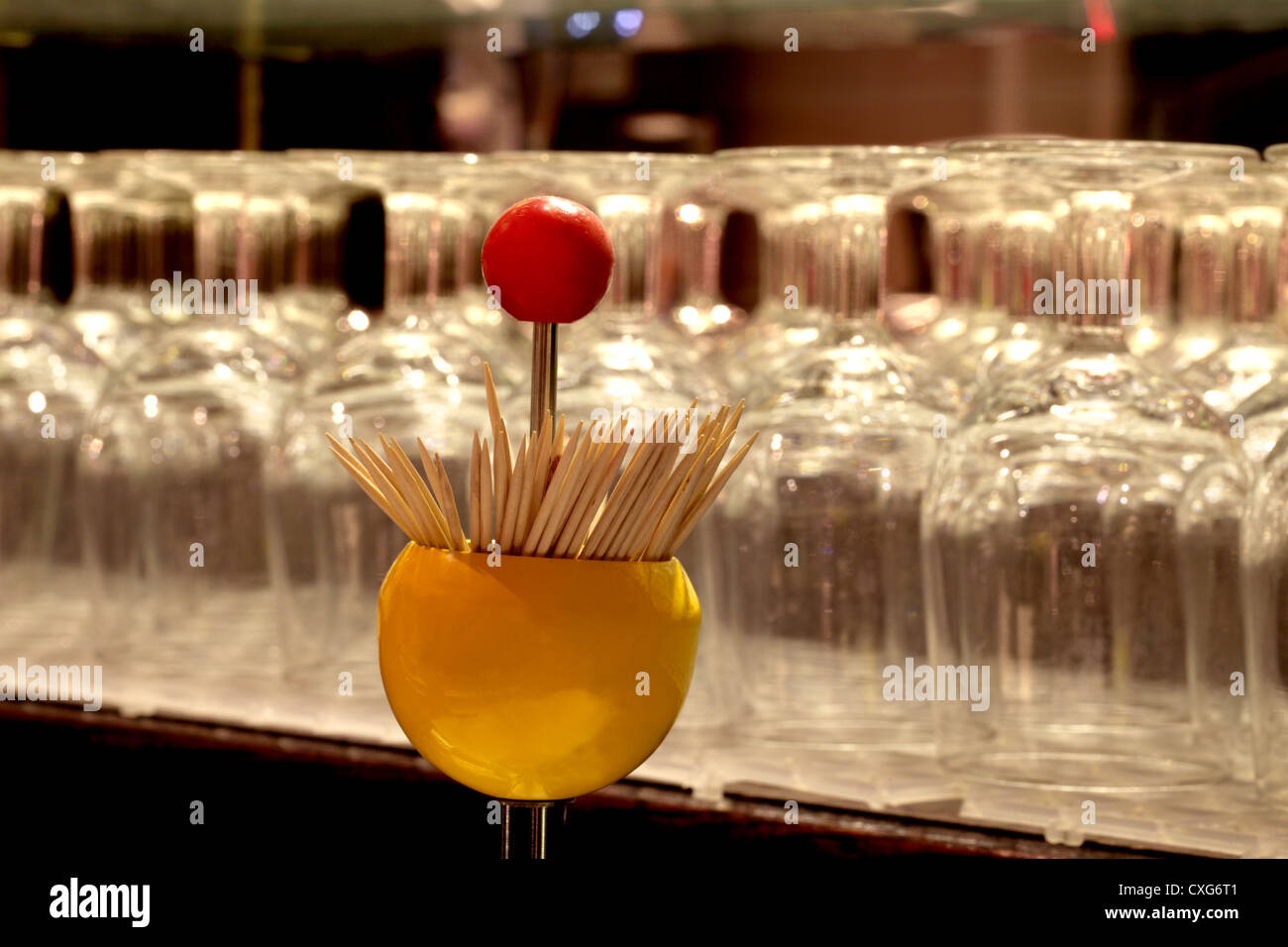 A container of cocktail sticks with a shelf full of drinking glasses in ...