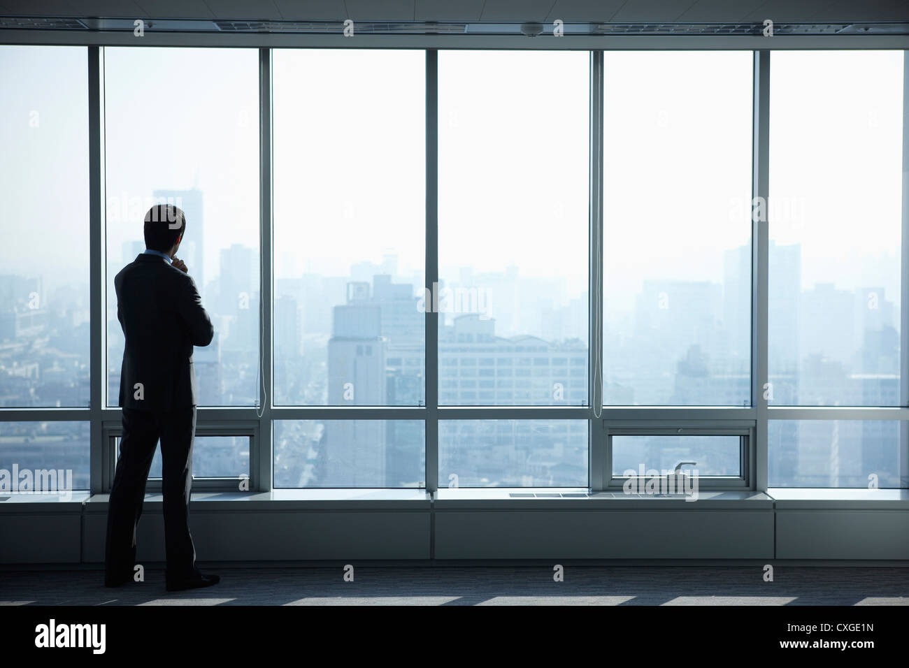 A businessman looking out a window in dark building Stock Photo - Alamy