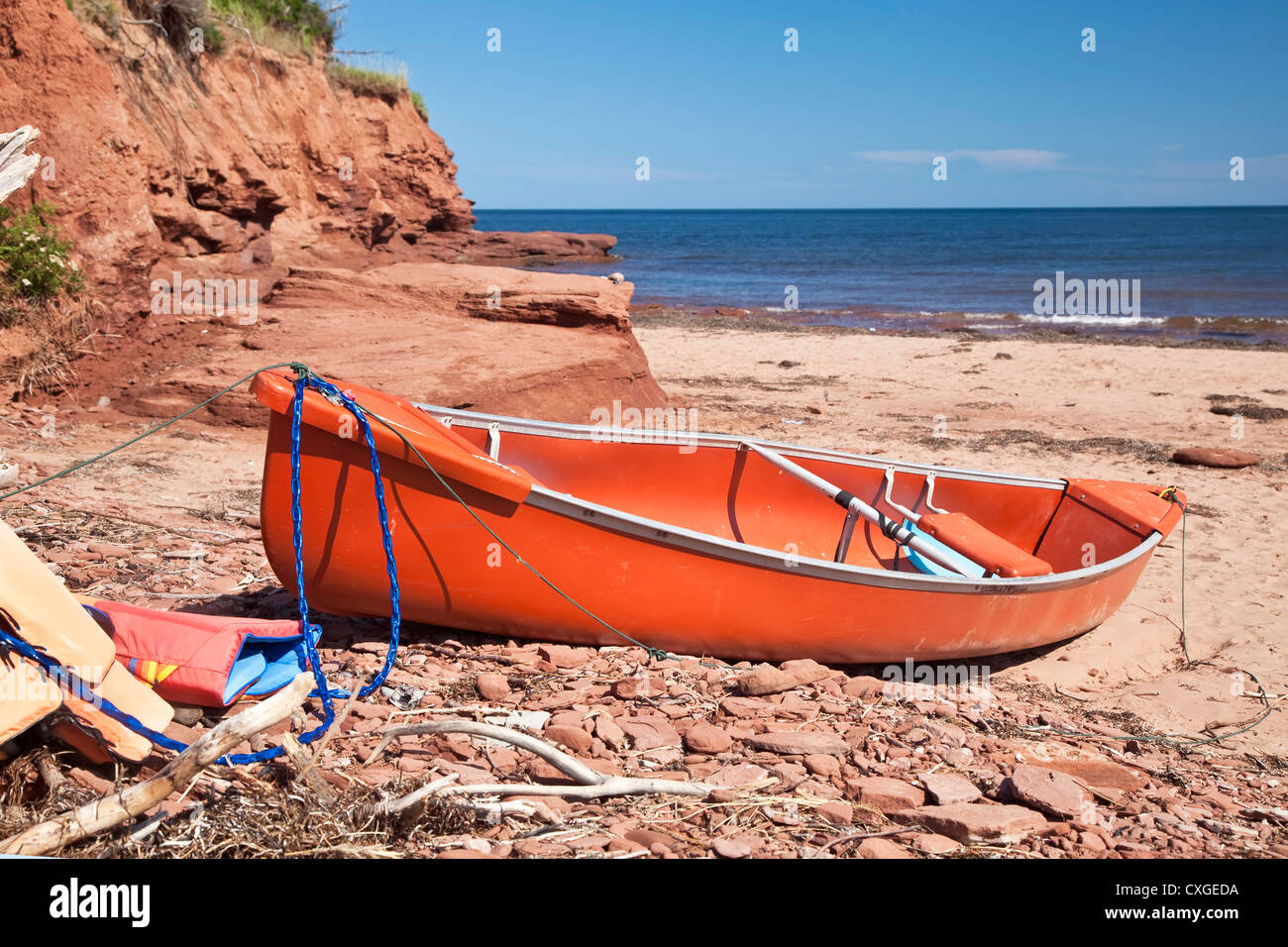 A canoe laying on a rocky beach beside a sandstone cliff on Cabot Beach ...